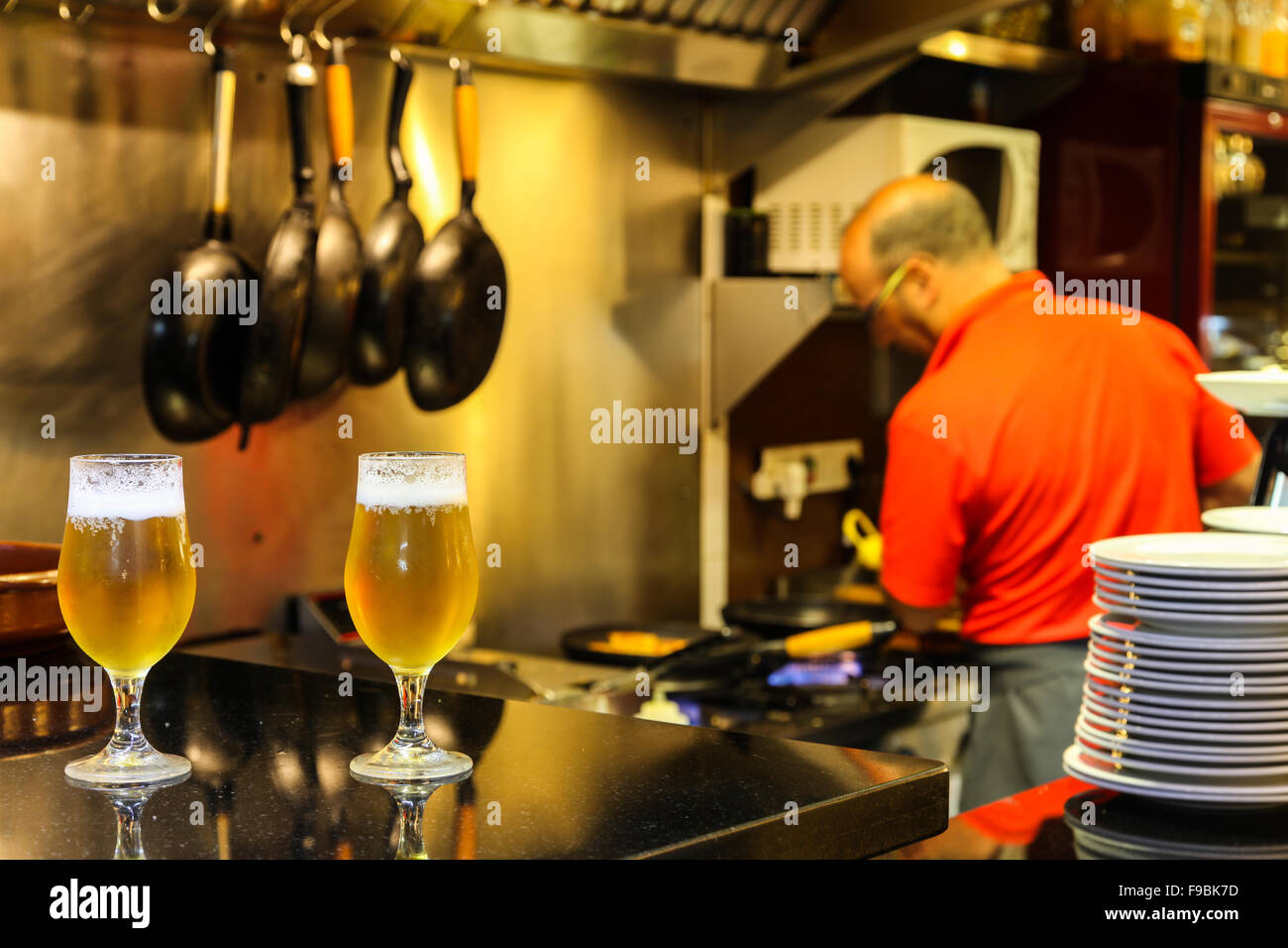 Two beers on a counter in a Spanish tapas bar with the chef cooking in ...