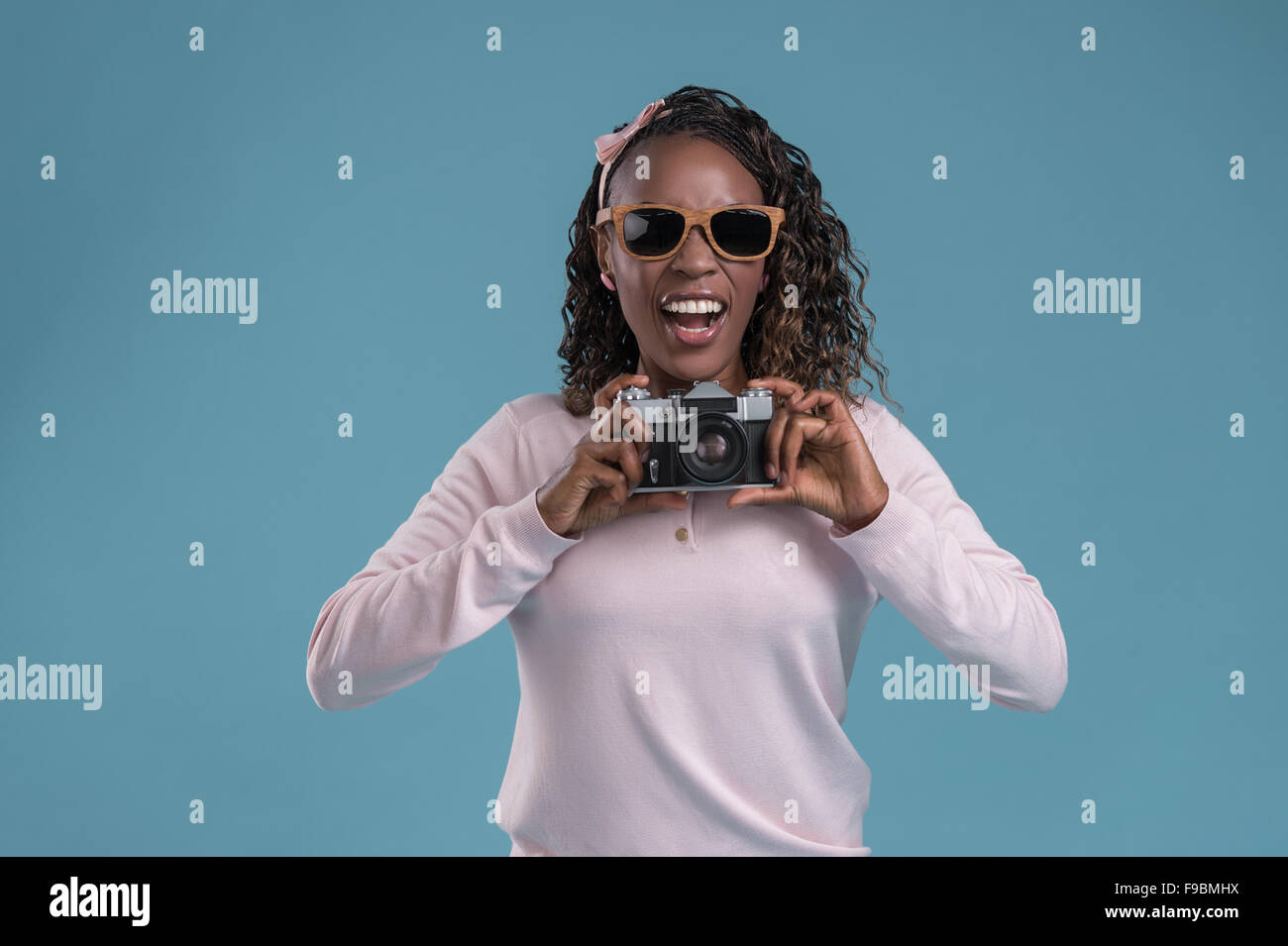 Beautiful young african woman using camera and photographing on blue ...