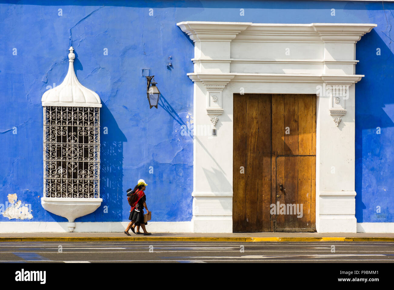 Peruvian women in traditional dress walk past a colonial-style building ...