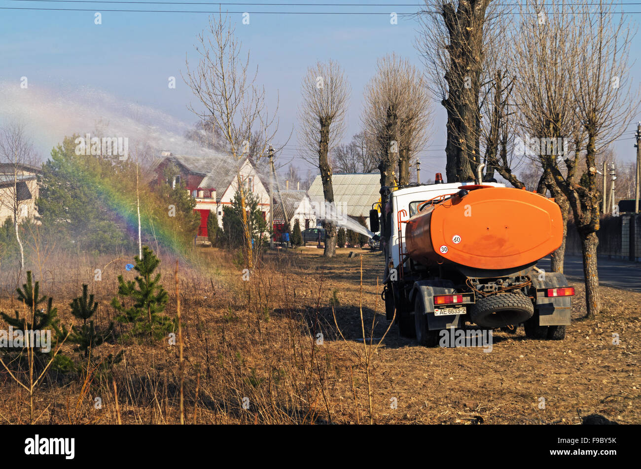 Spraying water on young trees in park from street sprinkler truck Stock ...