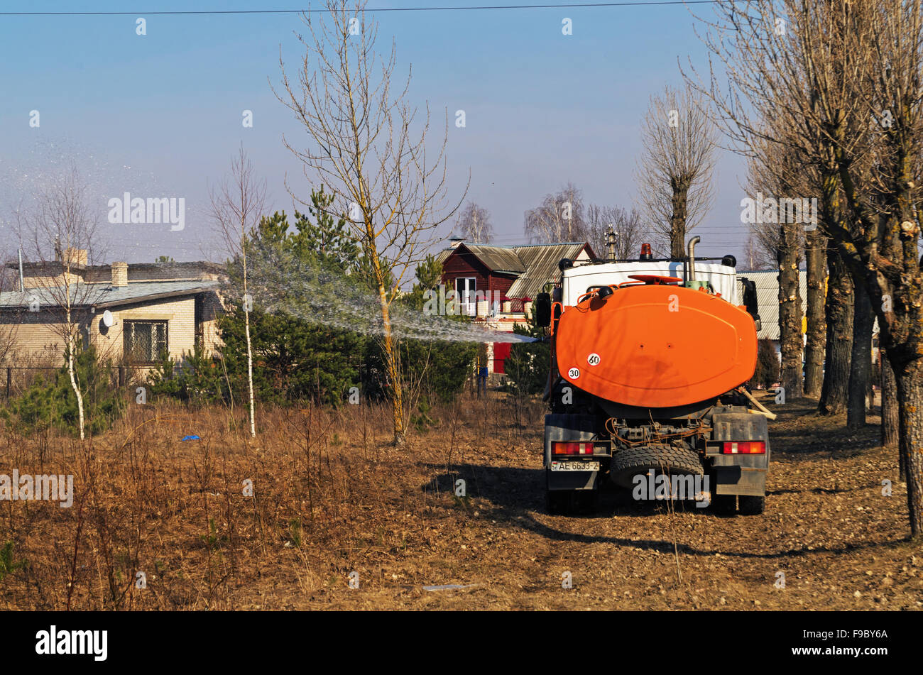 Spraying water on young trees in park from street sprinkler truck Stock ...