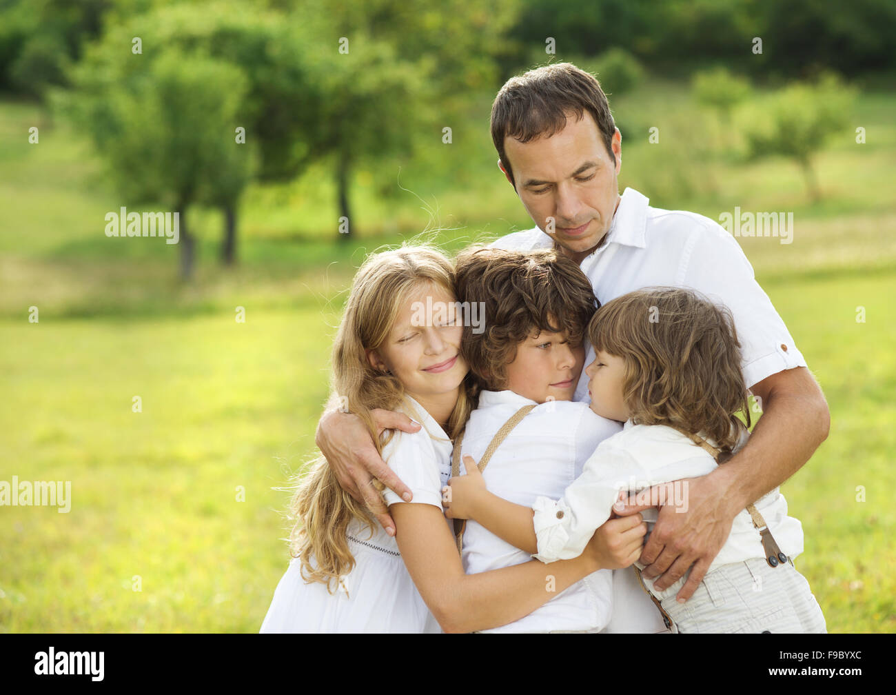 Children giving hugs to their dad on the meadow Stock Photo - Alamy