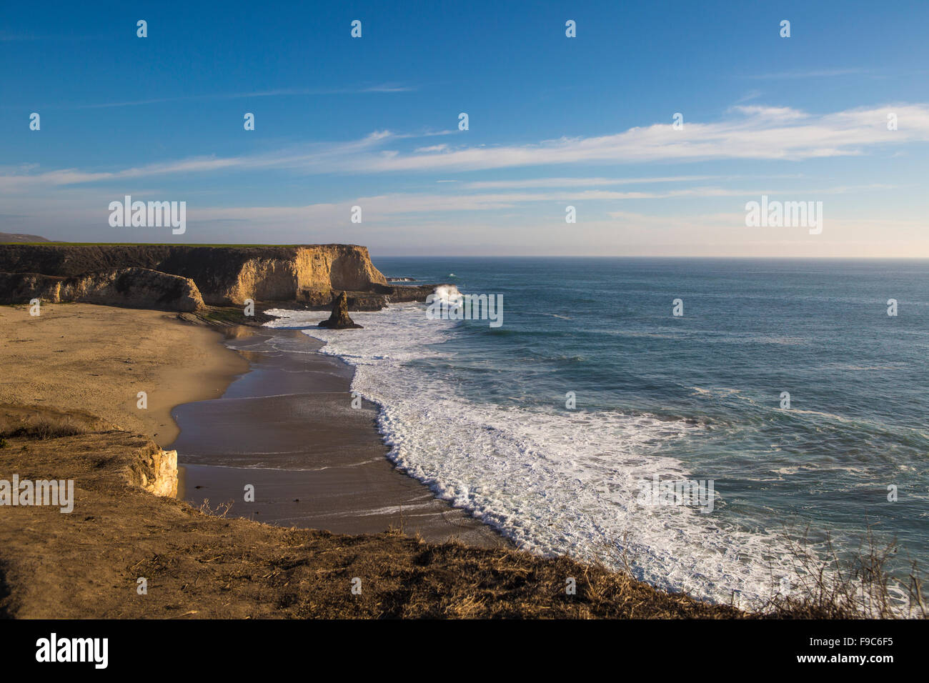 California cliffs with deep blue sky and wisps of cloud foaming waves ...