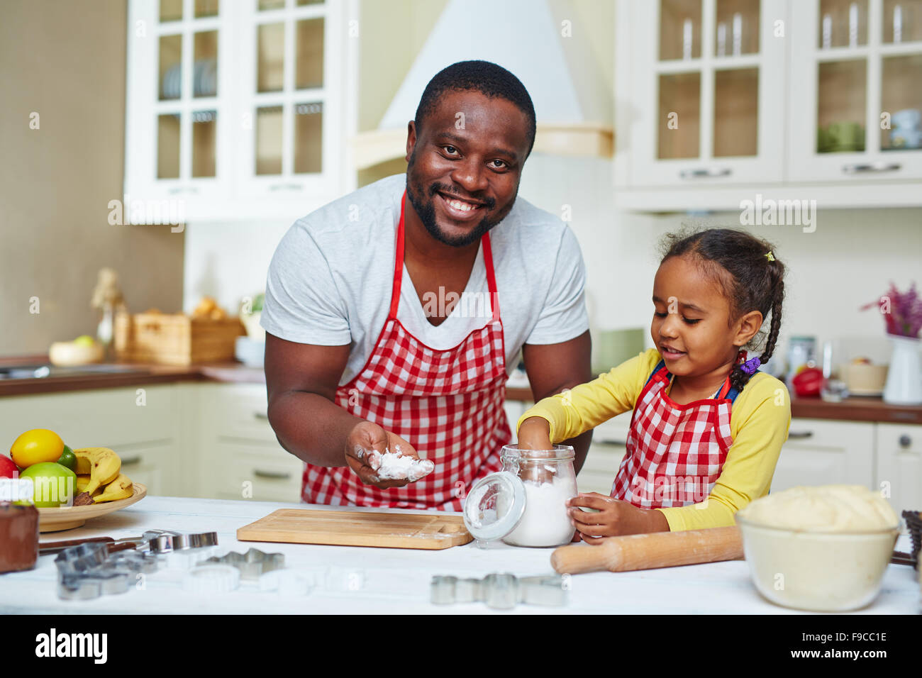 African-American man and his daughter in aprons cooking homemade pastry ...