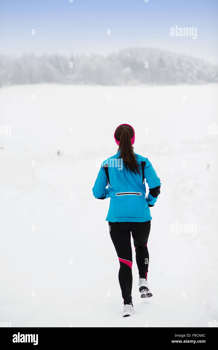 Athlete woman is running during winter training outside in cold snow ...