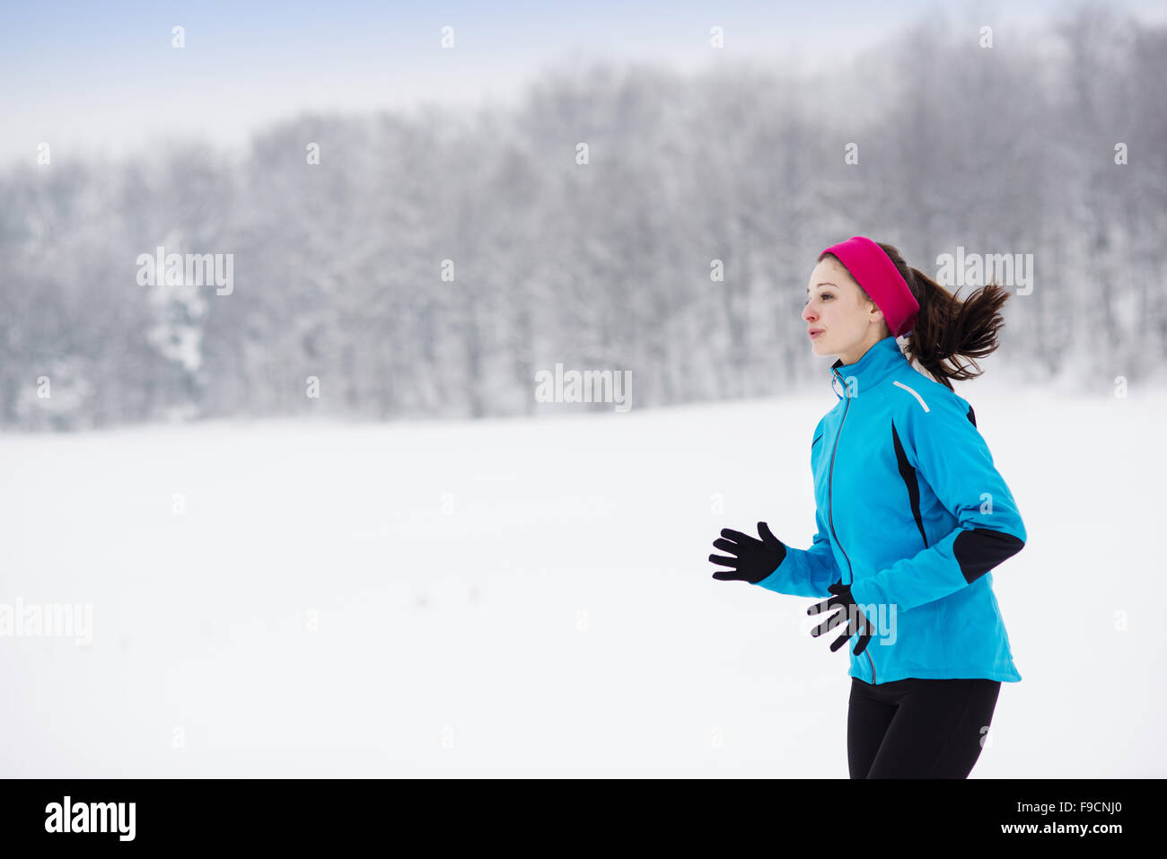 Athlete woman is running during winter training outside in cold snow ...