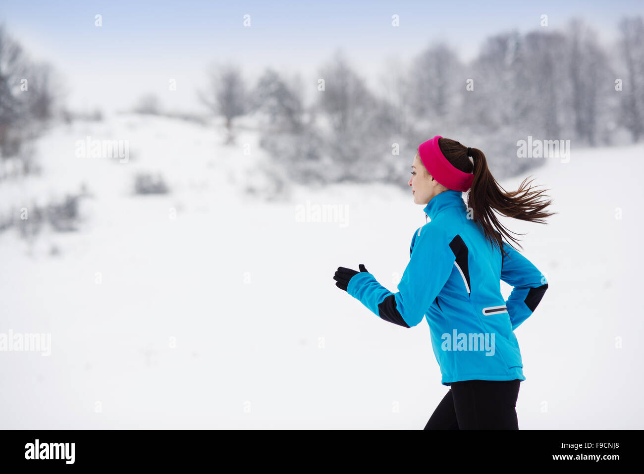 Athlete woman is running during winter training outside in cold snow ...