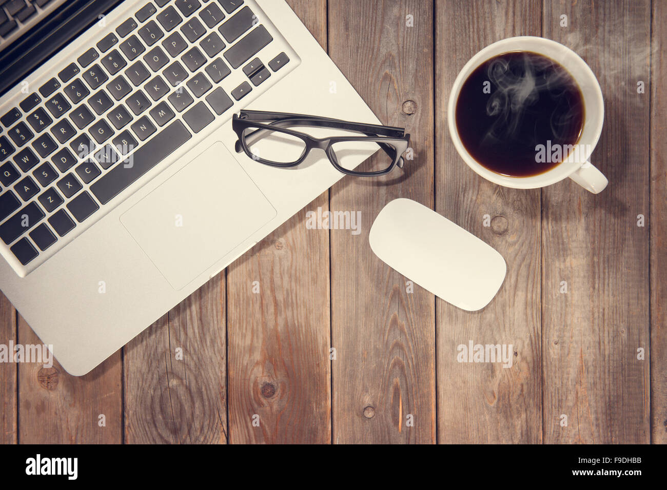 Top view work space with computer, cup of coffee and eyeglasses. Wooden ...