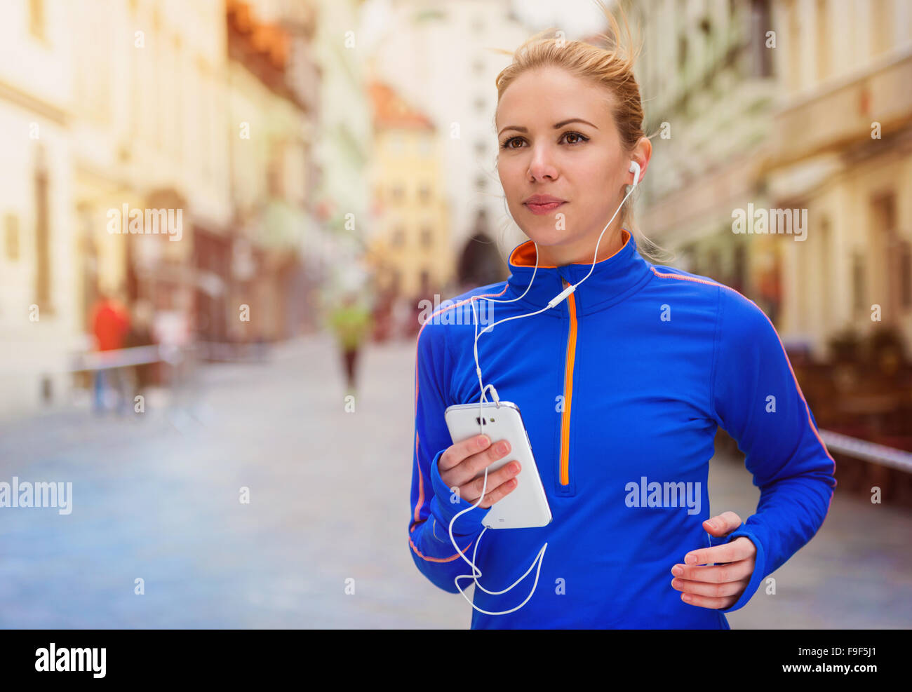 Beautiful young woman running in the city competition and listening to ...