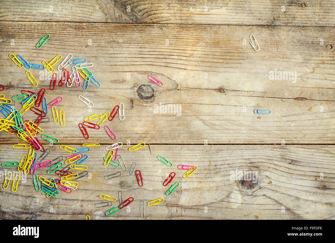 Colorful paperclips scattered on wooden floor background. View from ...