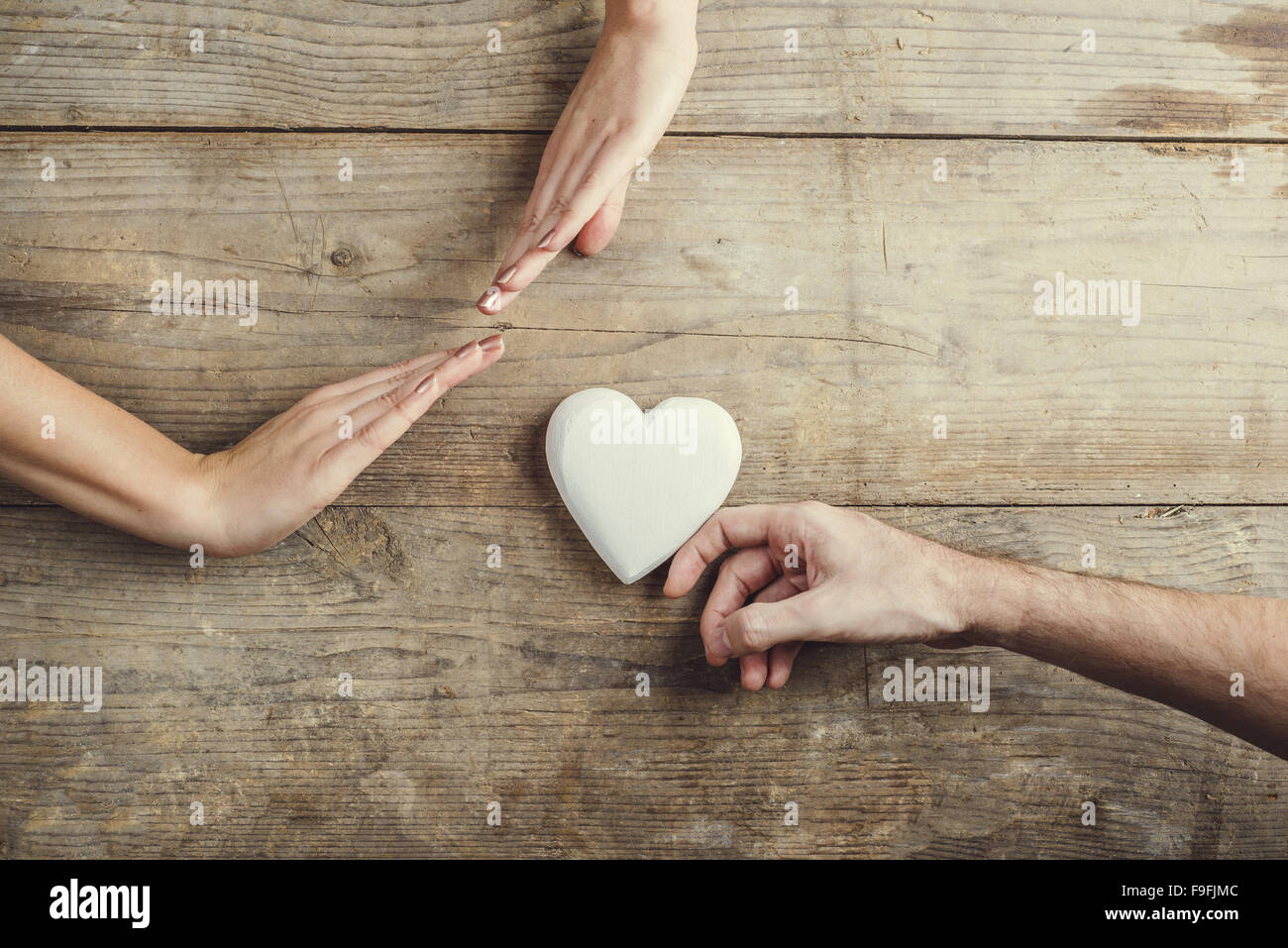 Man offering a white heart tenderly to a woman. Studio shot on a wooden ...