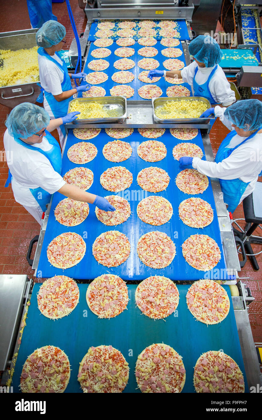 Staff on the production line put pinapple topping on frozen pizzas at ...