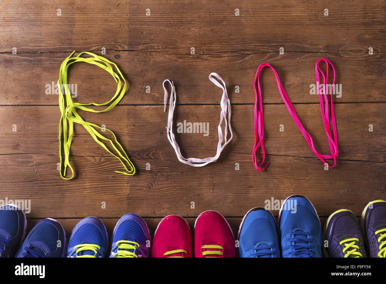 Five pairs of running shoes and shoelaces run sign on a wooden floor ...