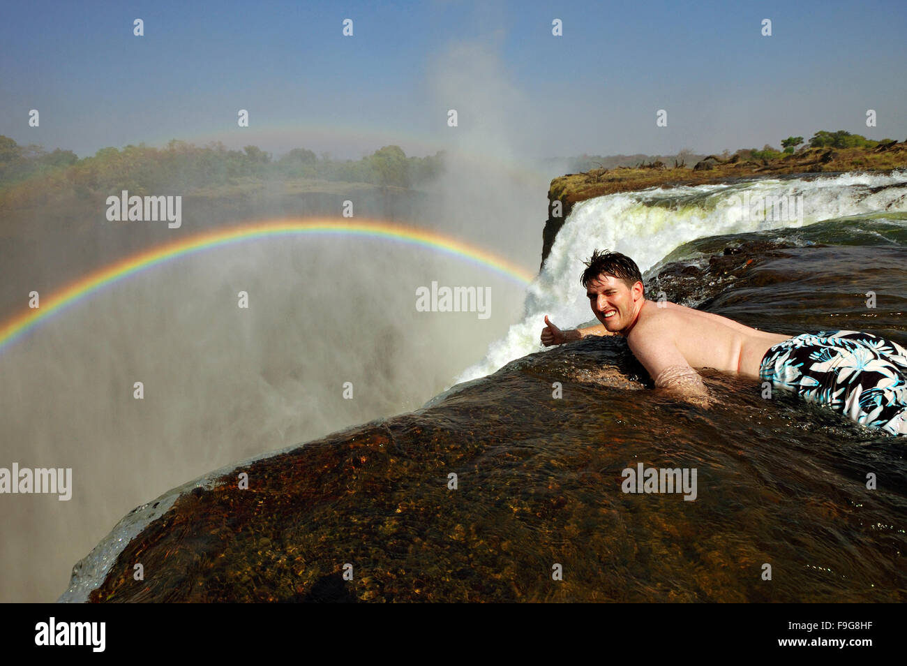 Smiling caucasian man giving thumbs up at the edge of Victoria Falls in ...