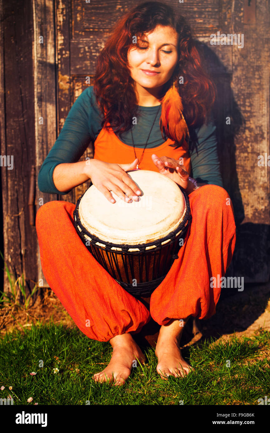 Young barefoot lady drummer playing on her djembe drum on rustic wooden ...