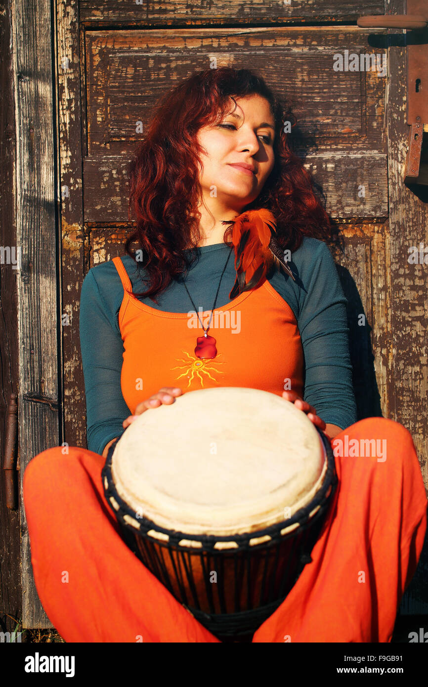 Young lady drummer with her djembe drum on rustic wooden door ...