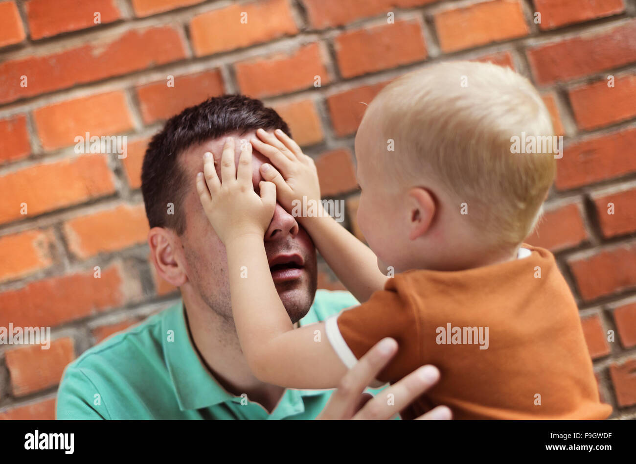 Father and son making funny faces together on a brick wall background ...