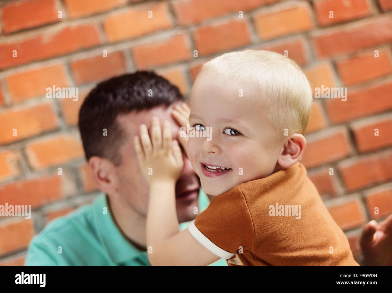Father and son making funny faces together on a brick wall background ...