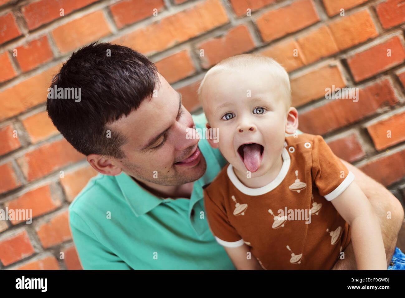 Father and son making funny faces together on a brick wall background ...