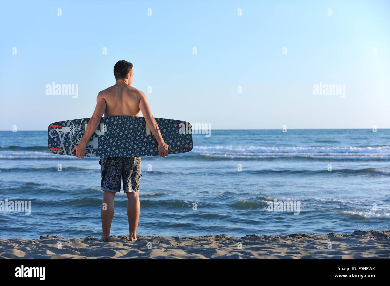 Portrait of a strong young surf man at beach on sunset in a ...