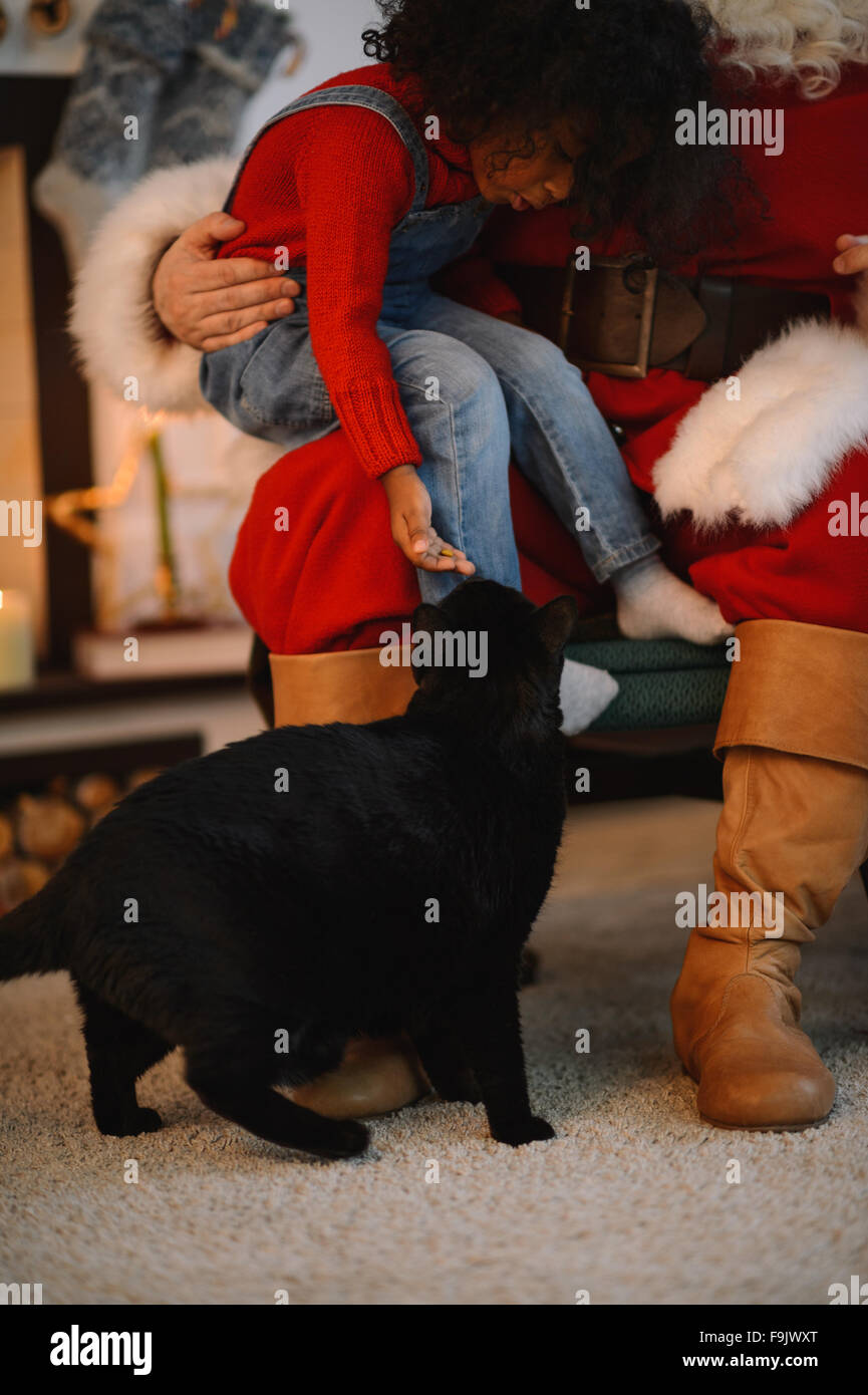 Santa Claus feeding a cat with cute african child near the fireplace ...