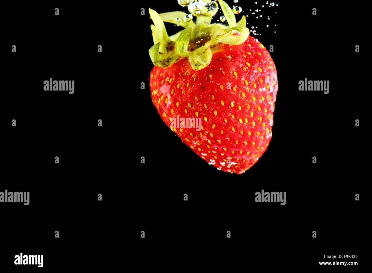Strawberry falling into water at black background Stock Photo - Alamy