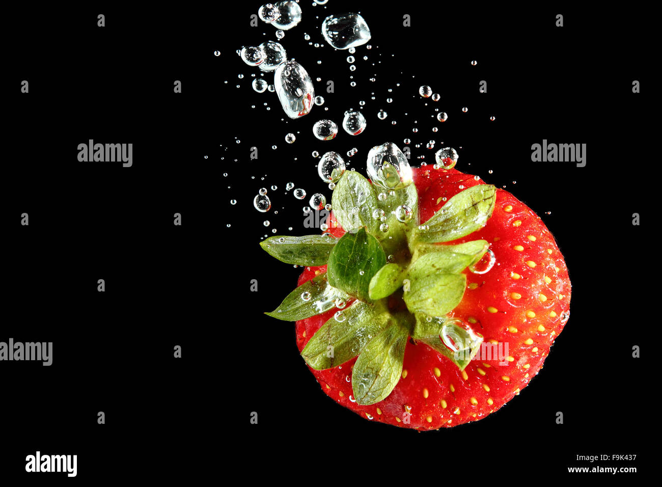 Strawberry falling into water at black background Stock Photo - Alamy