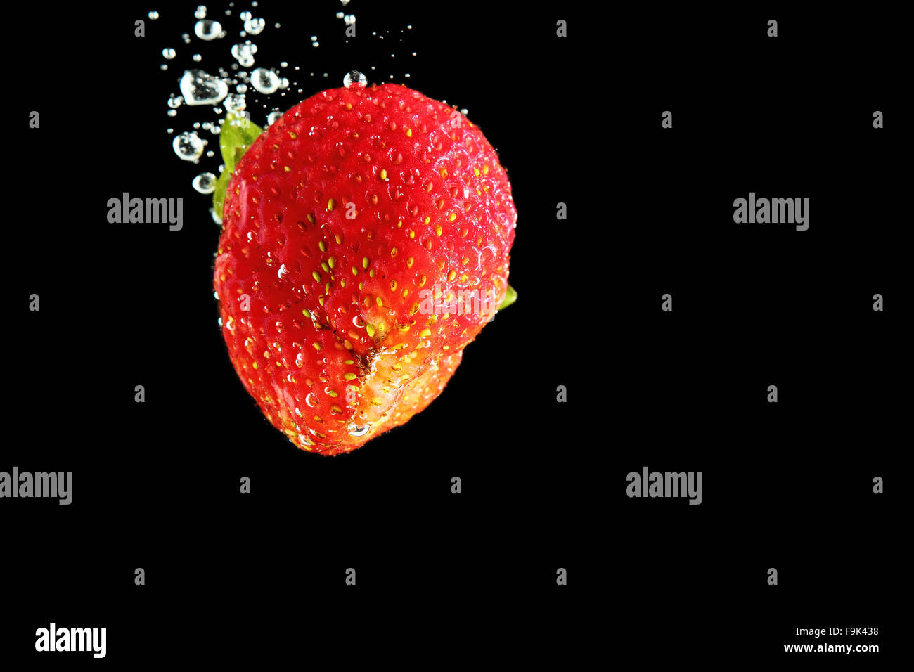 Strawberry falling into water at black background Stock Photo - Alamy