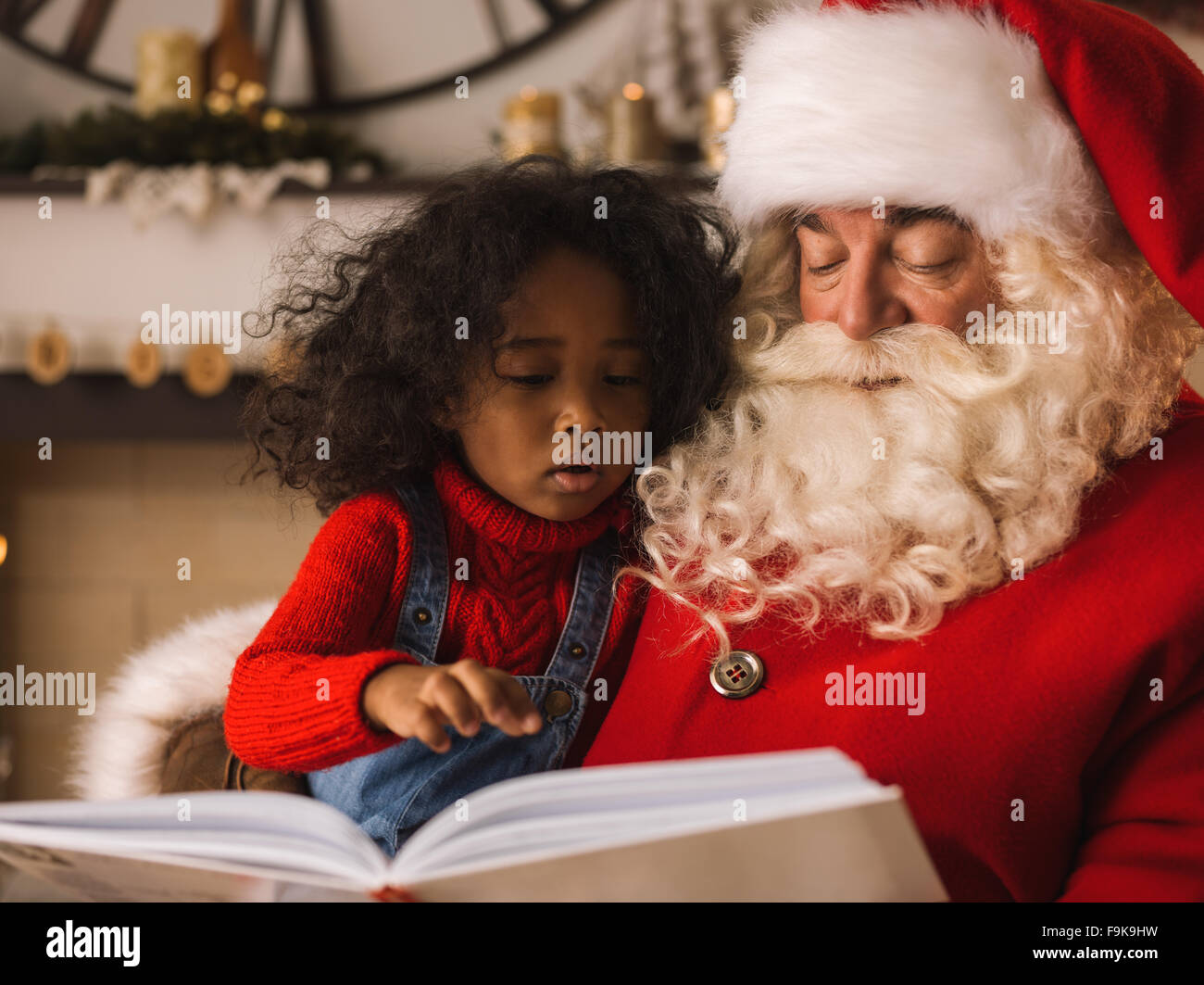 Santa Claus reading a book with cute african child near the fireplace ...
