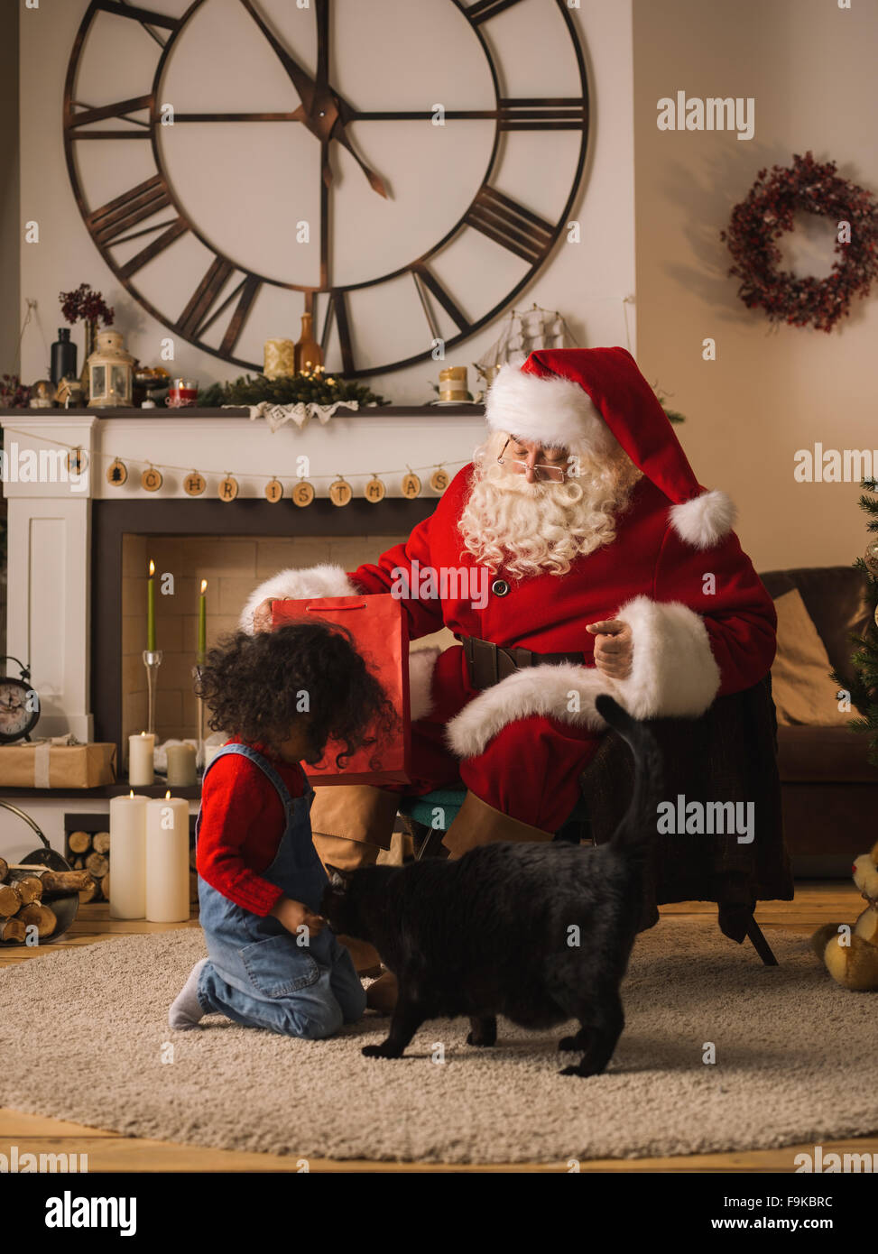 Santa Claus feeding a cat with cute african child near the fireplace ...