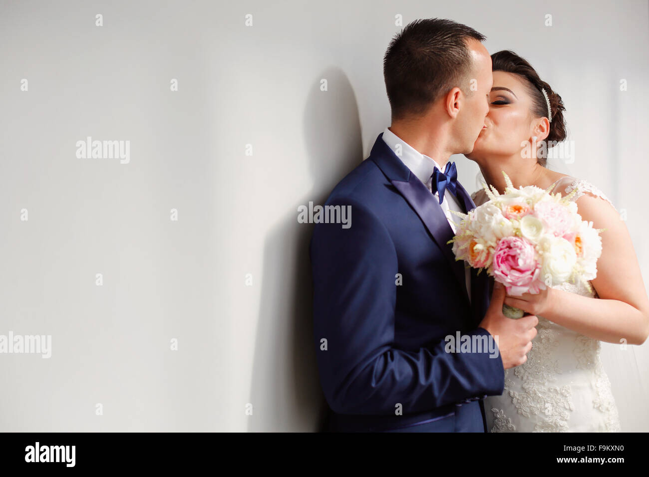 Beautiful bridal couple kissing next to white wall Stock Photo - Alamy
