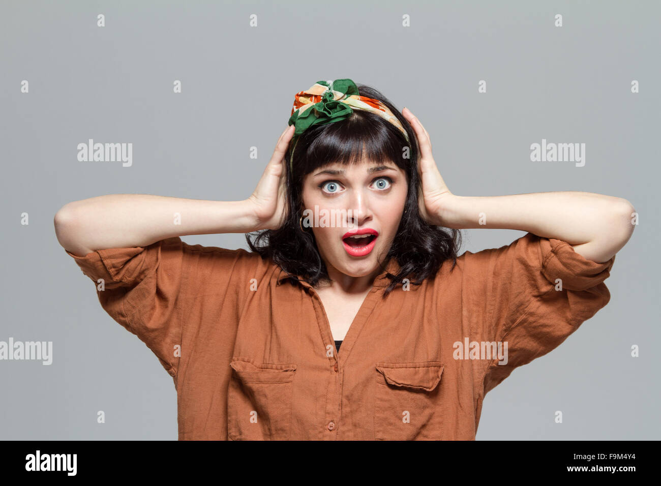 Shocked dazed young woman with opened mouth holding head by hands ...