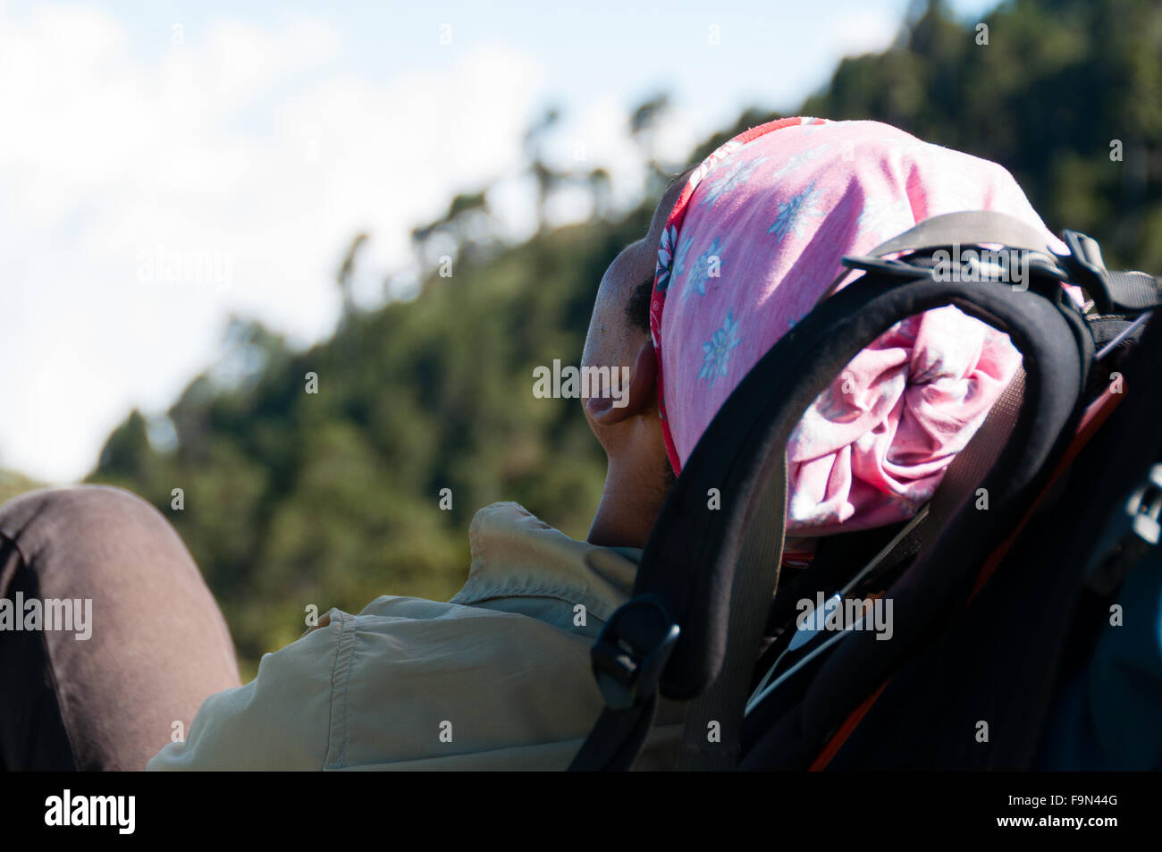 Young Man with pink bandana resting laying on his backpack in the sun ...