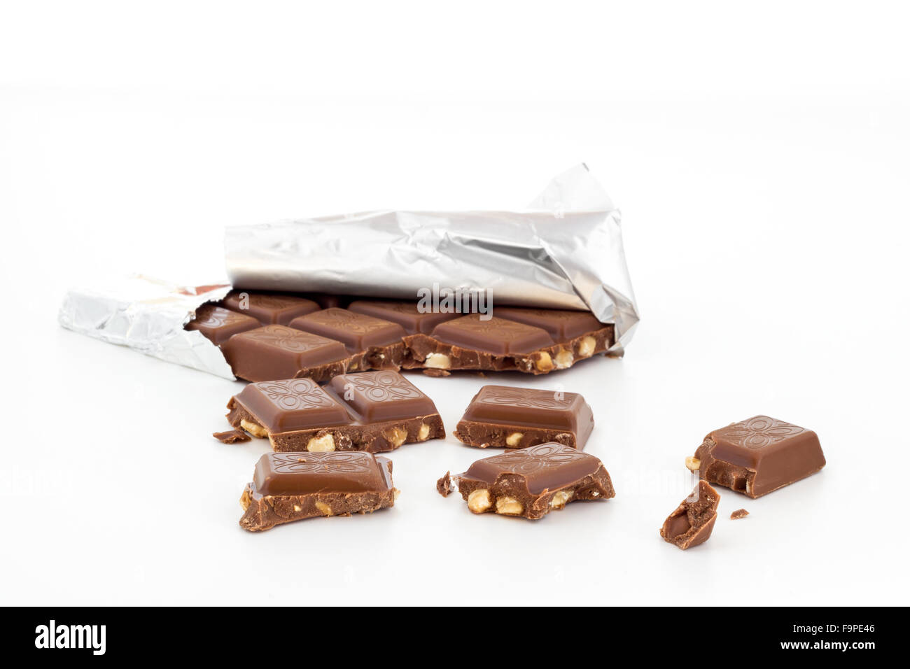 Bar of milk chocolate with hazelnuts, with pieces and flakes scattered ...