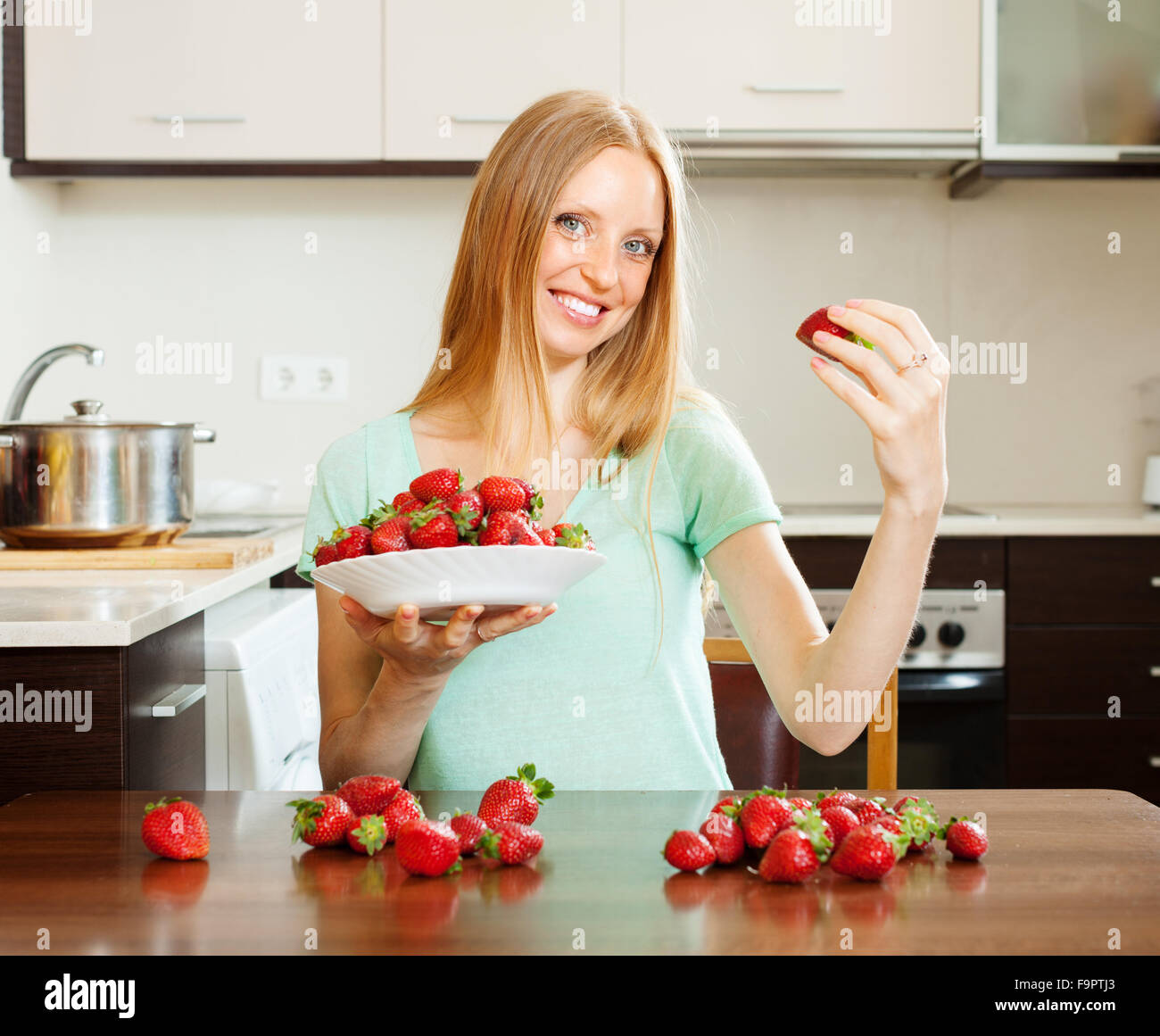 Positive blonde long-haired woman wstrawberries in home Stock Photo - Alamy