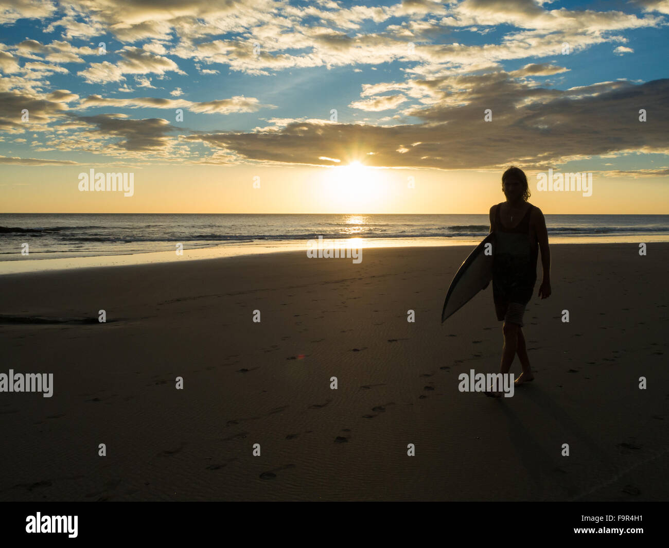 Surfer walks on the beach at the sunrise or sunset Stock Photo - Alamy