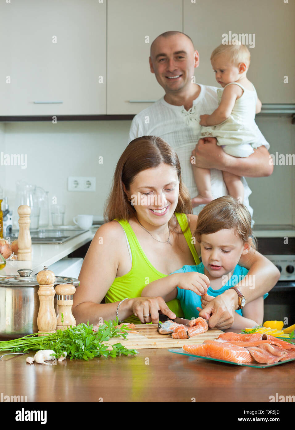Happy family of four making red fresh fish at home Stock Photo - Alamy