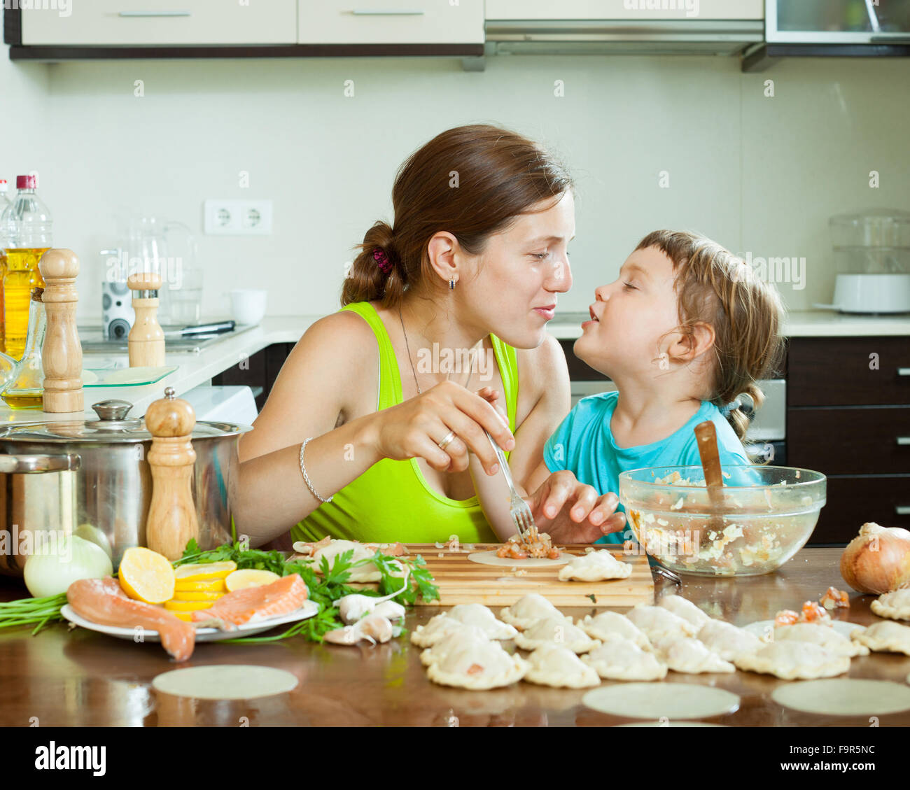 Positive woman with girl cooking fish dumplings together at home ...