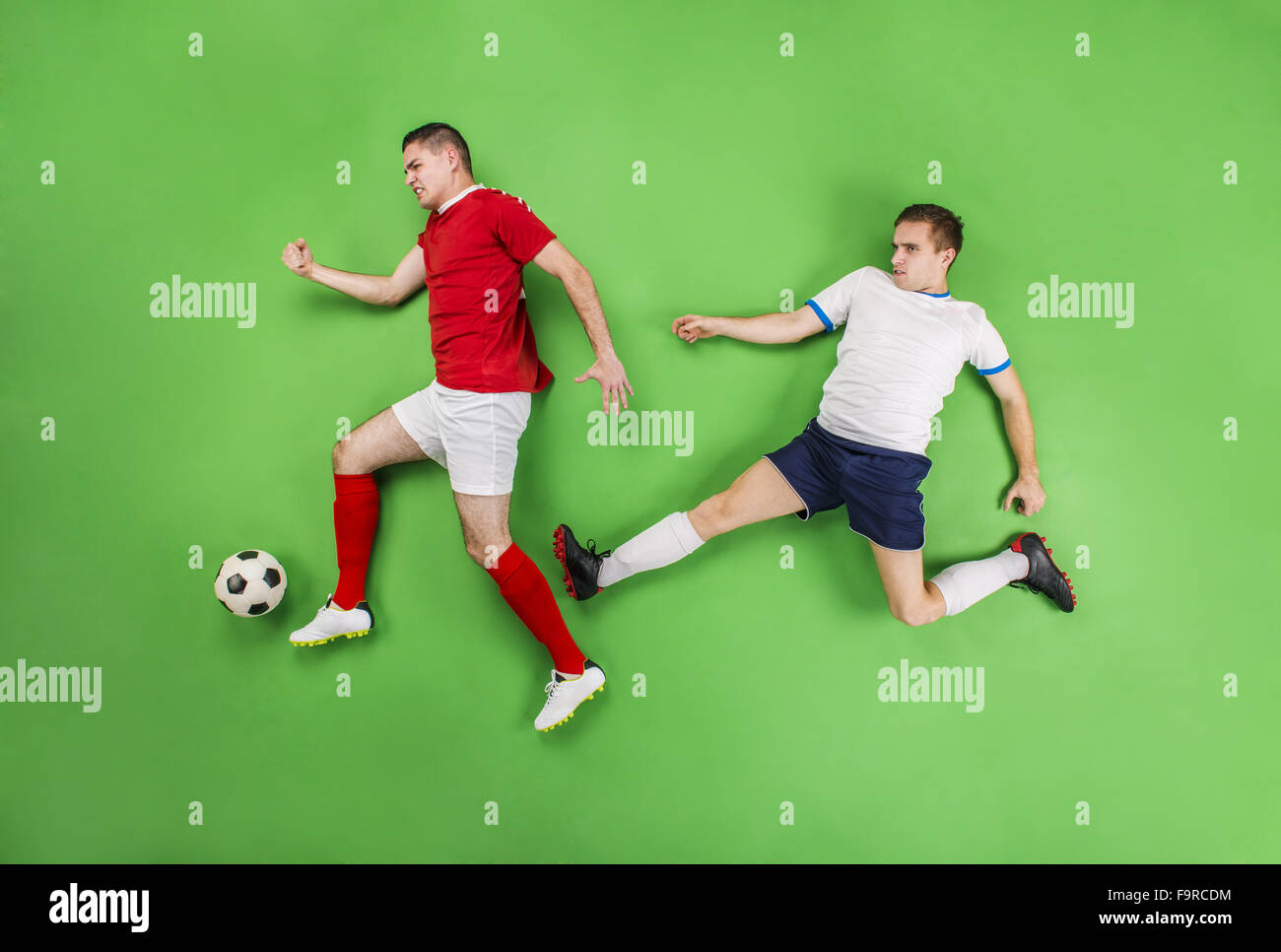 Two football players fighting for a ball. Studio shot on a green ...