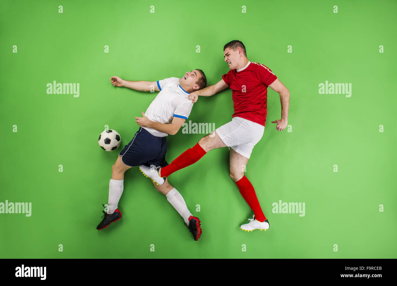 Two football players fighting for a ball. Studio shot on a green ...