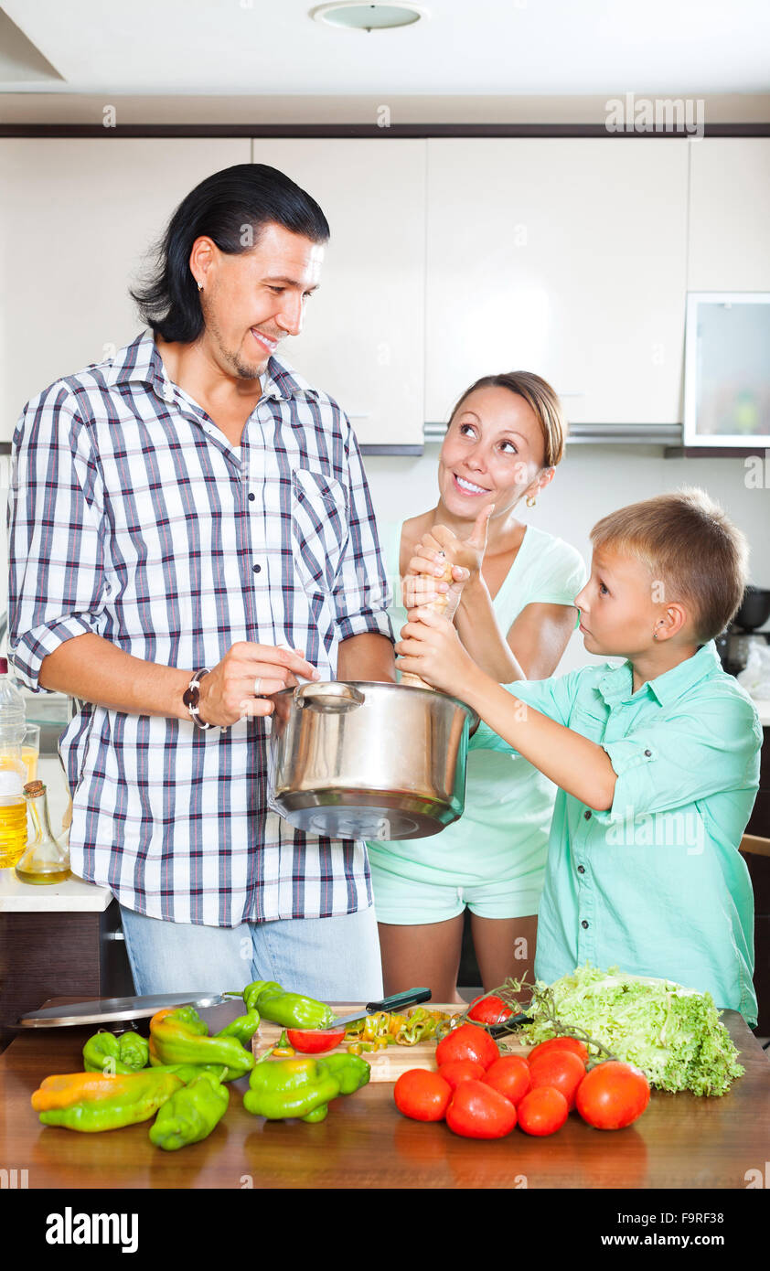Happy couple with teenager son cooking veggy lunch in home kitchen ...