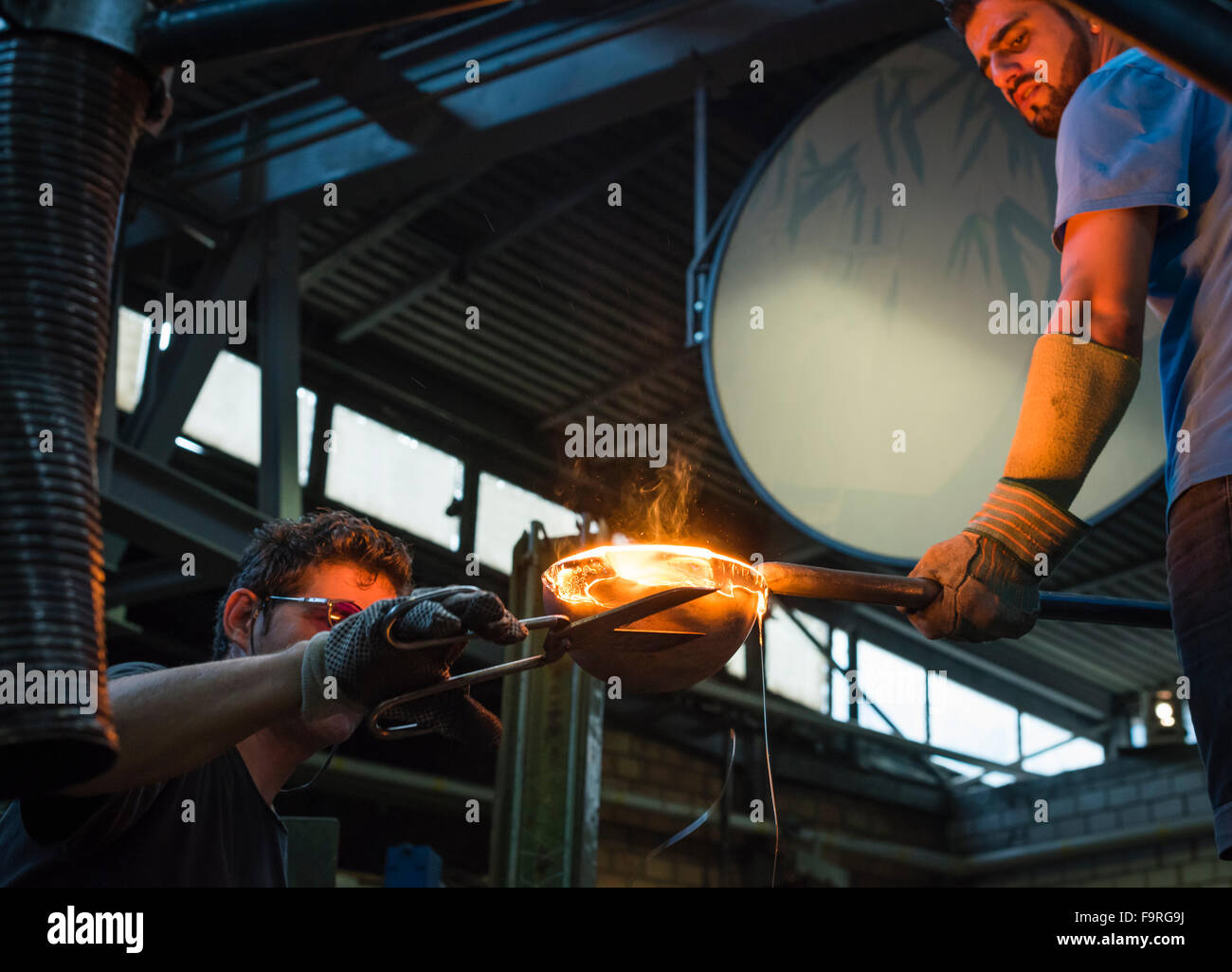 Glassblowers working in front of the furnace at the glass factory ...