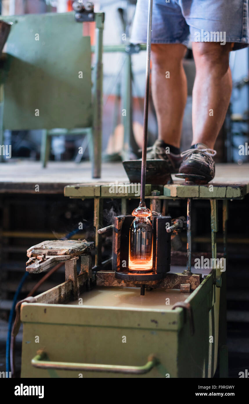 Melted glass, glowing red hot, is being shaped in a mould at the ...