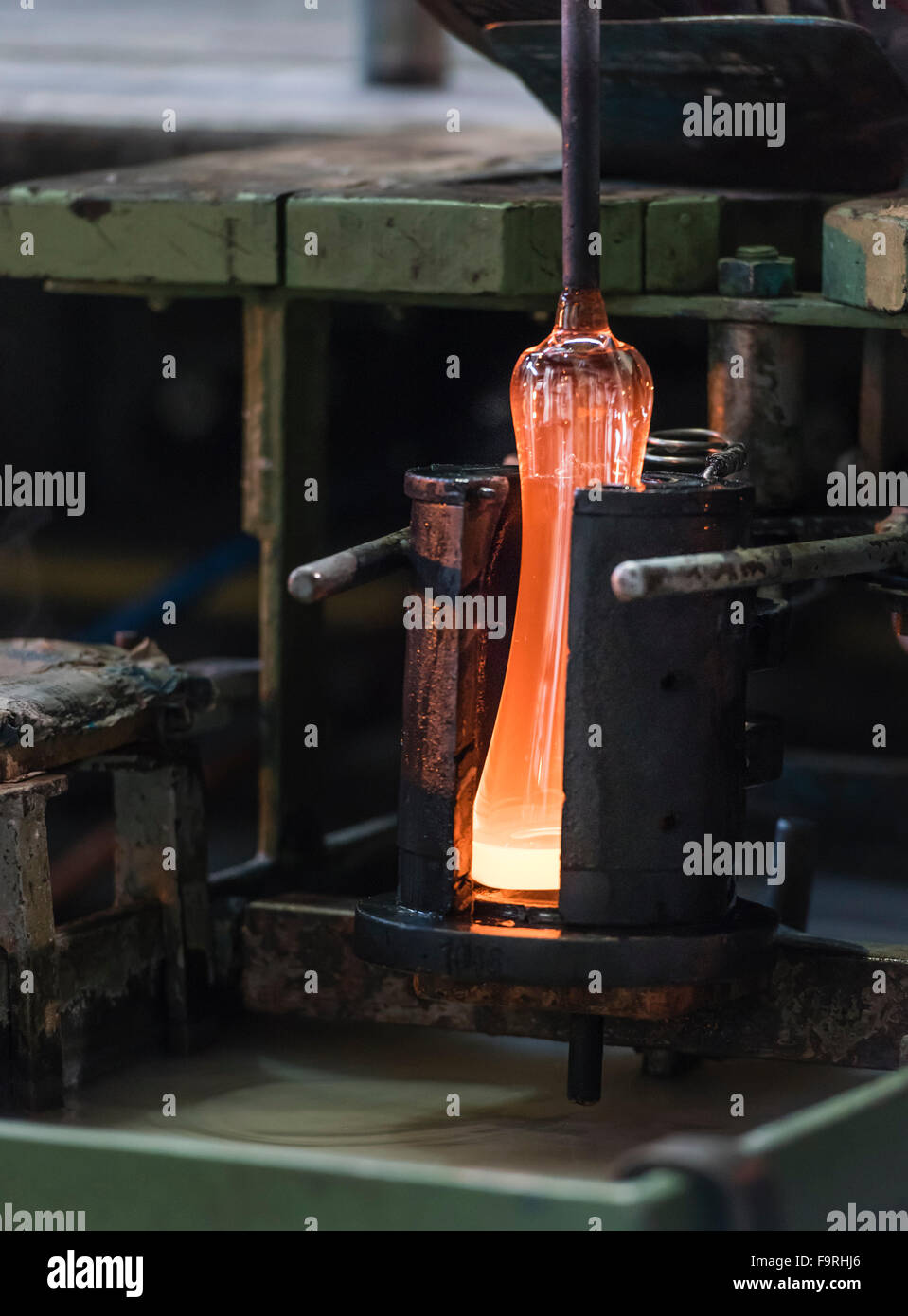 Melted glass, glowing red hot, is being shaped in a mould at the ...