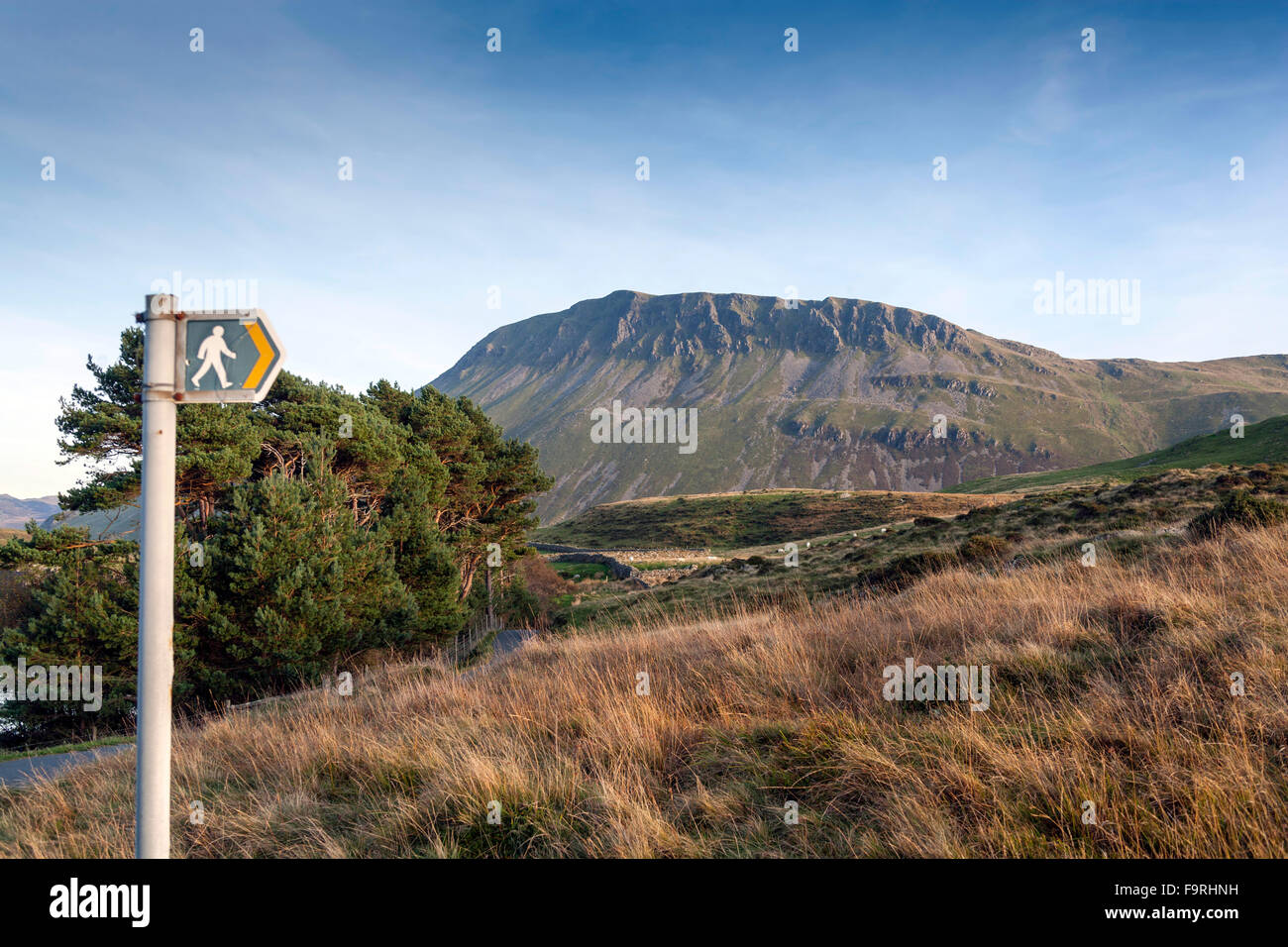 A weather worn footpath sign on open grassland with the steep slopes of ...
