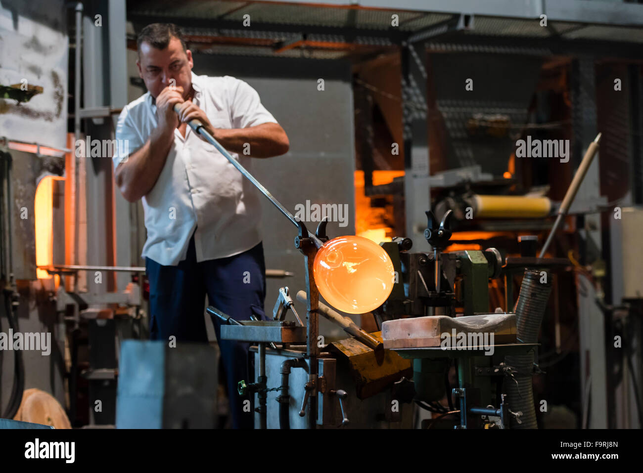 A glassblower at work in front of the furnace of the traditional ...