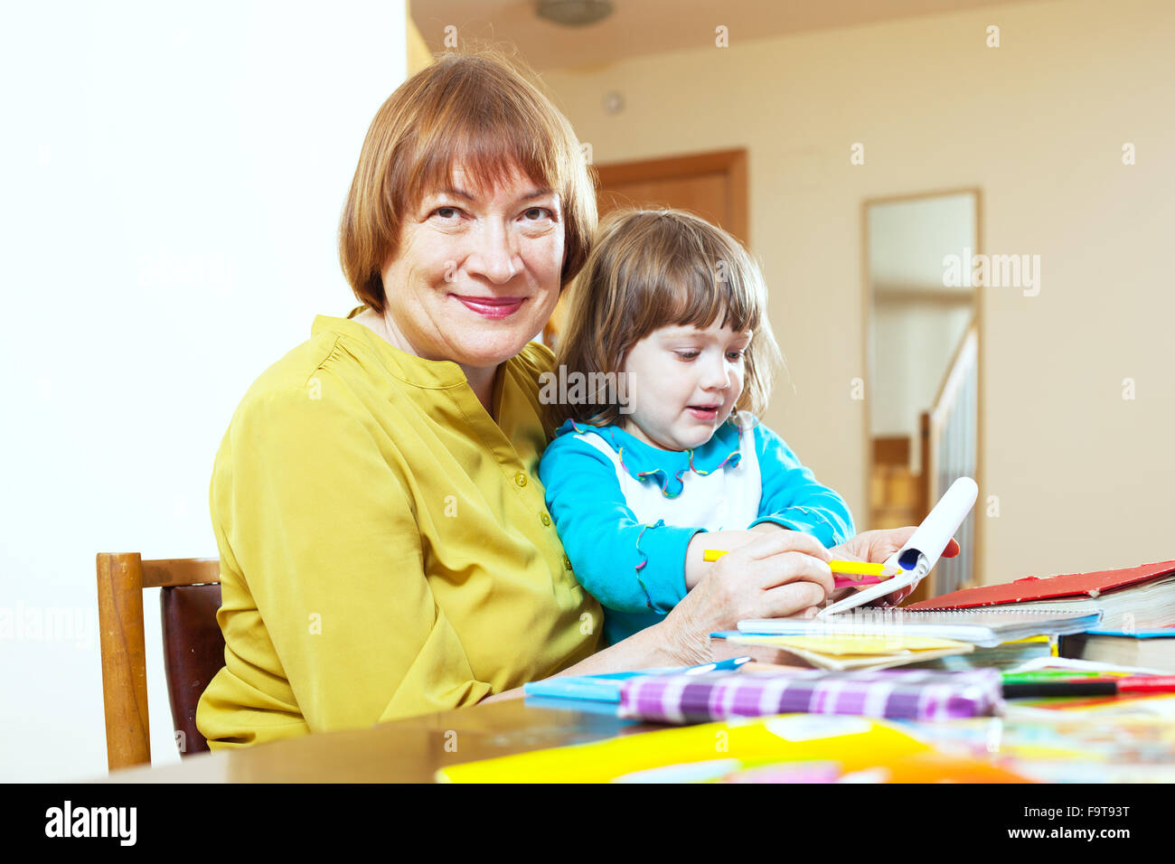 Happy mature woman and child drawing with colored pencils together at ...