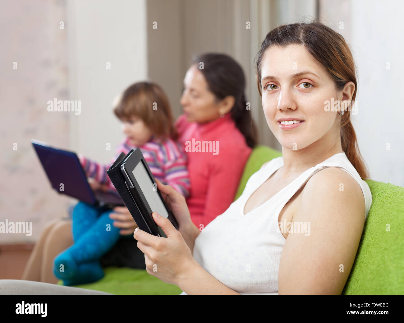 Family of three generations using electronic devices on sofa in home ...