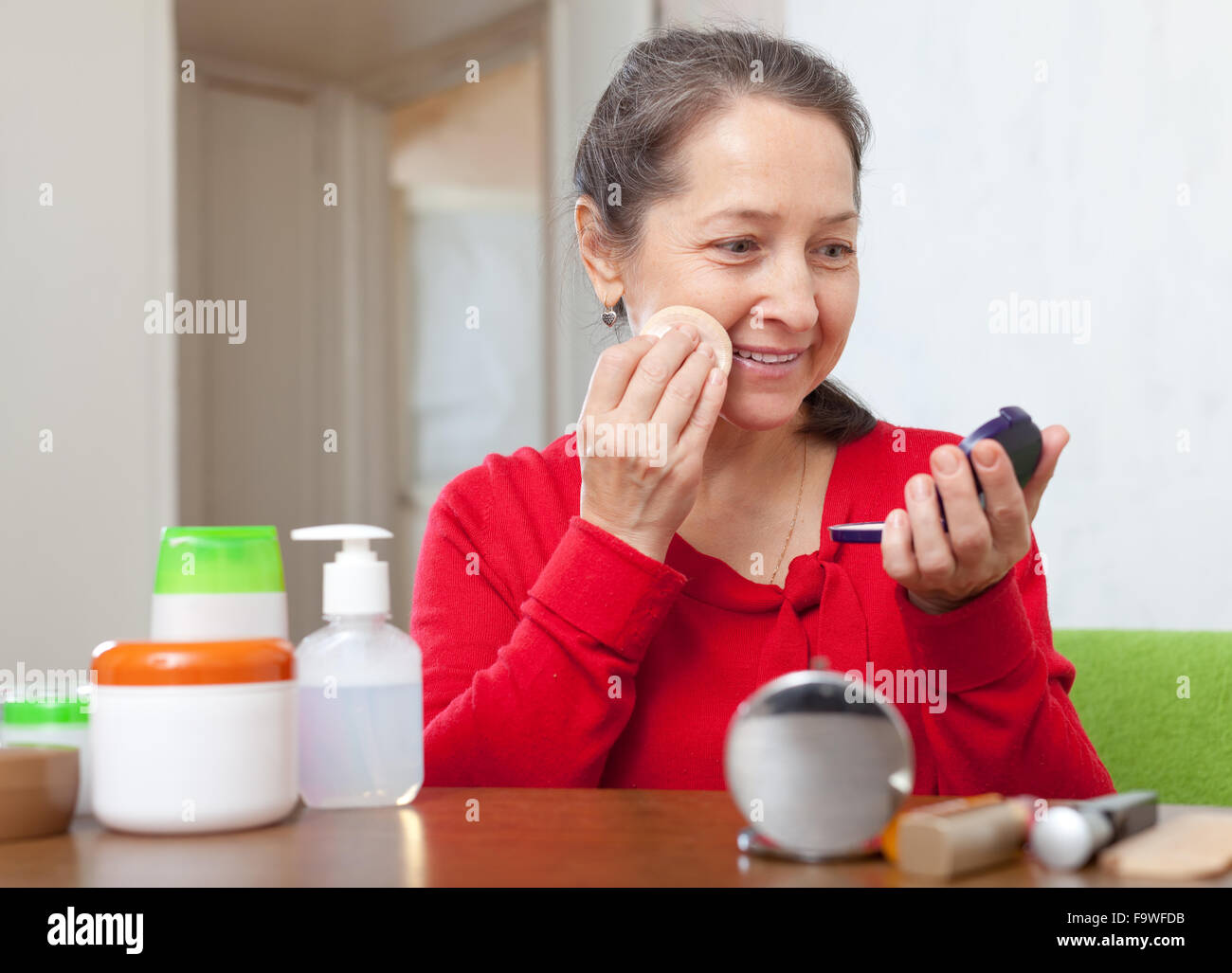 Smiling mature woman in red dress putting facepowder on her face Stock ...