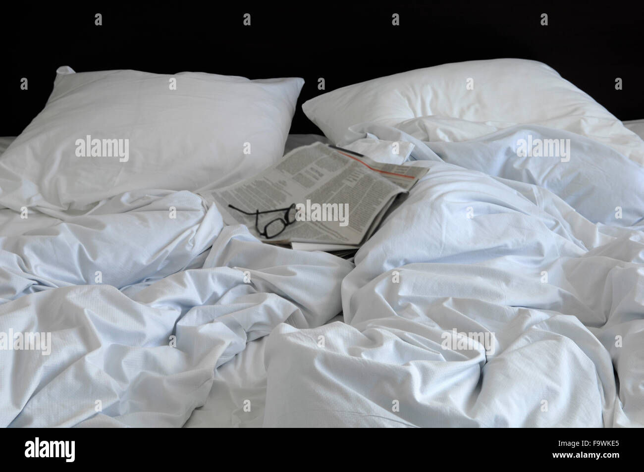 Rumpled bed with glasses and newspaper Stock Photo - Alamy